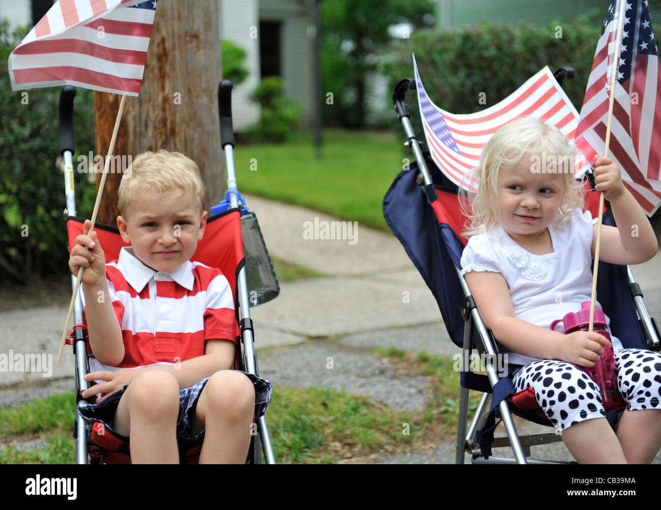 A young boy and girl in strollers and waving American Flags watch the ...