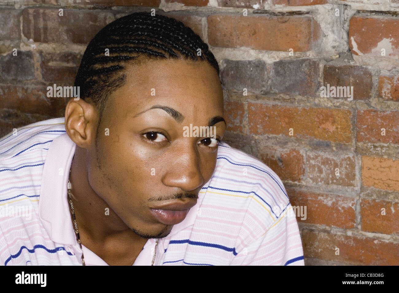 Portrait of a young man in hip-hop fashion sitting against brick wall ...
