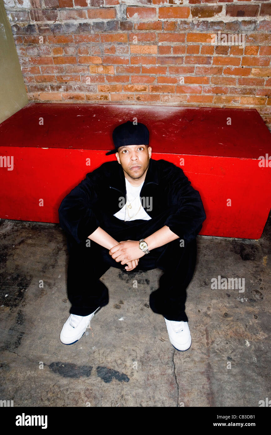 Portrait of a young man in hip-hop fashion sitting against brick wall ...