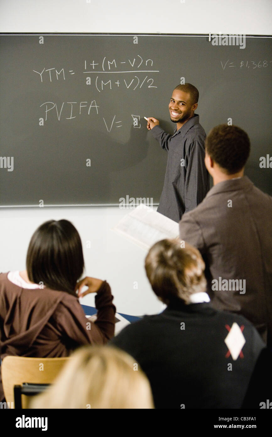 Student writing on the chalkboard in front of classmates and teacher ...