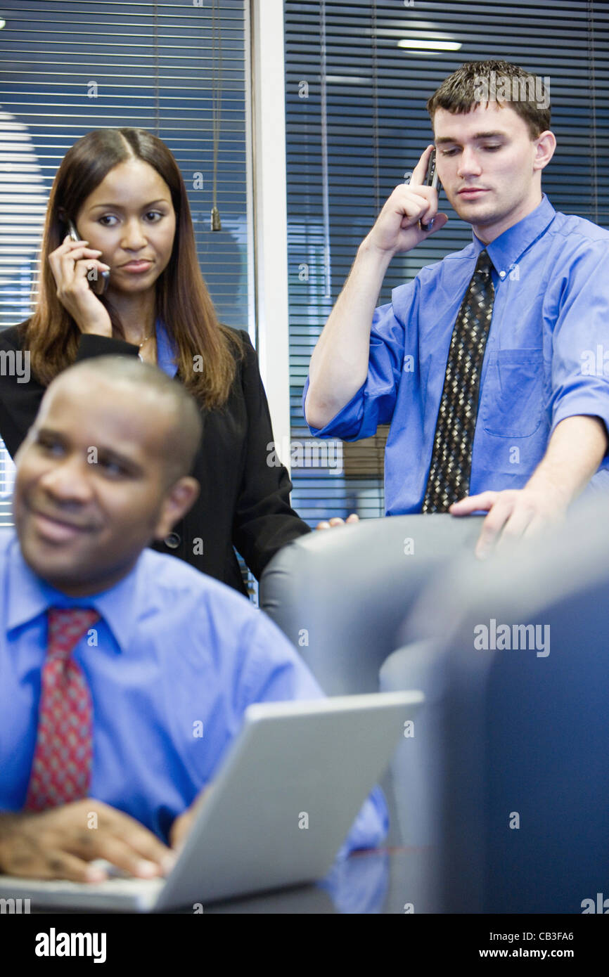 Business man and woman using mobile phone while colleague uses laptop ...
