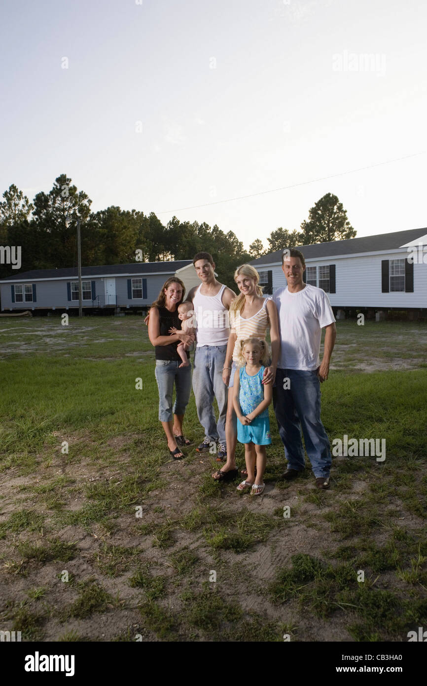 Portrait of two blue-collar families standing in front of trailer homes ...