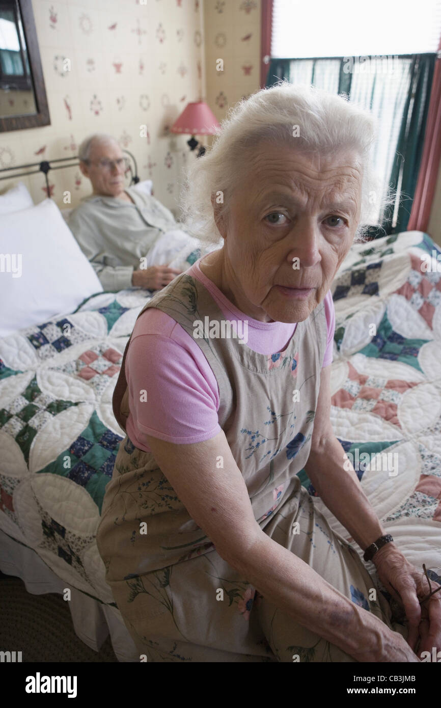 Worried senior woman sitting on bed with bedridden senior man Stock ...