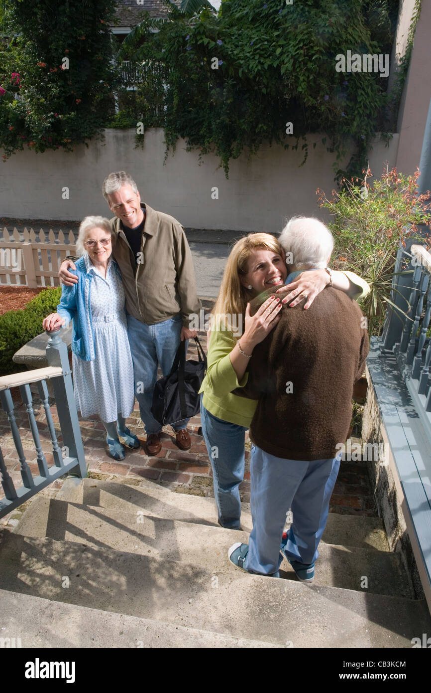 Woman cheerfully hugging senior man on steps while man and senior woman ...
