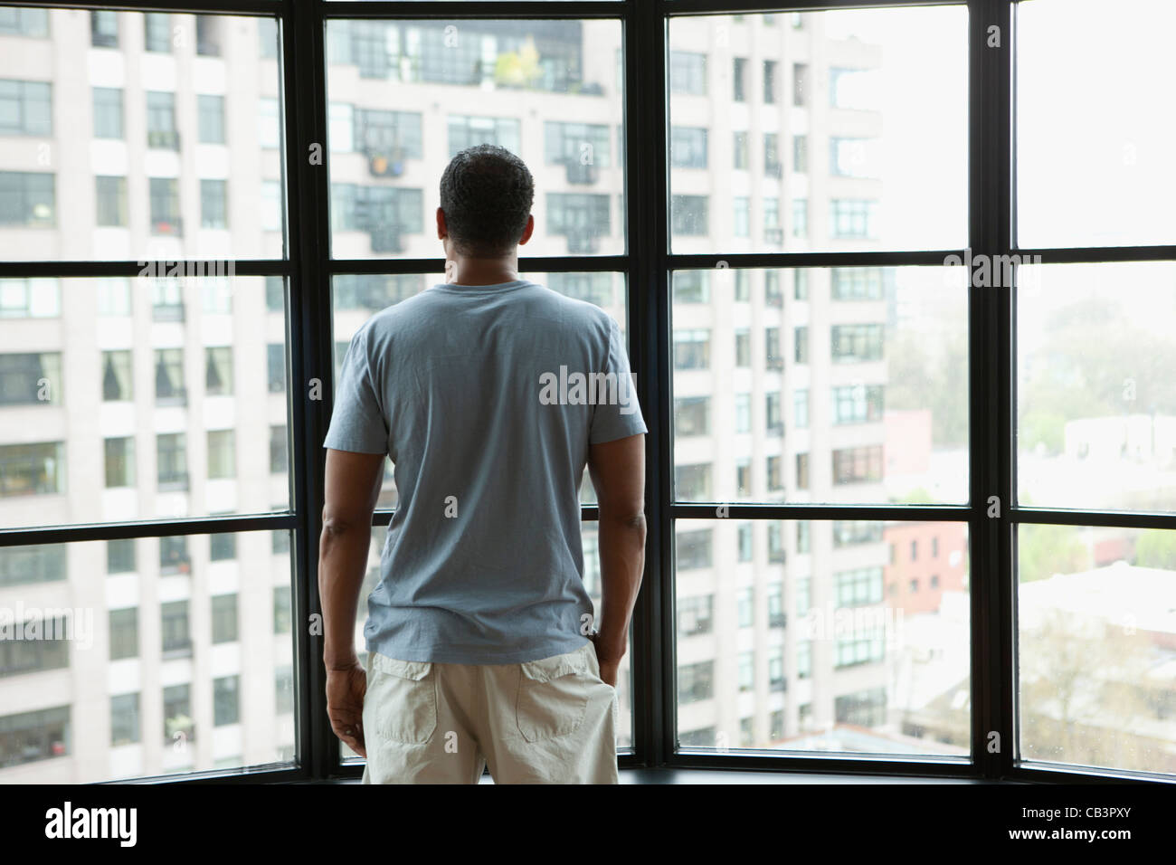 Man looking out on city from his loft apartment Stock Photo - Alamy