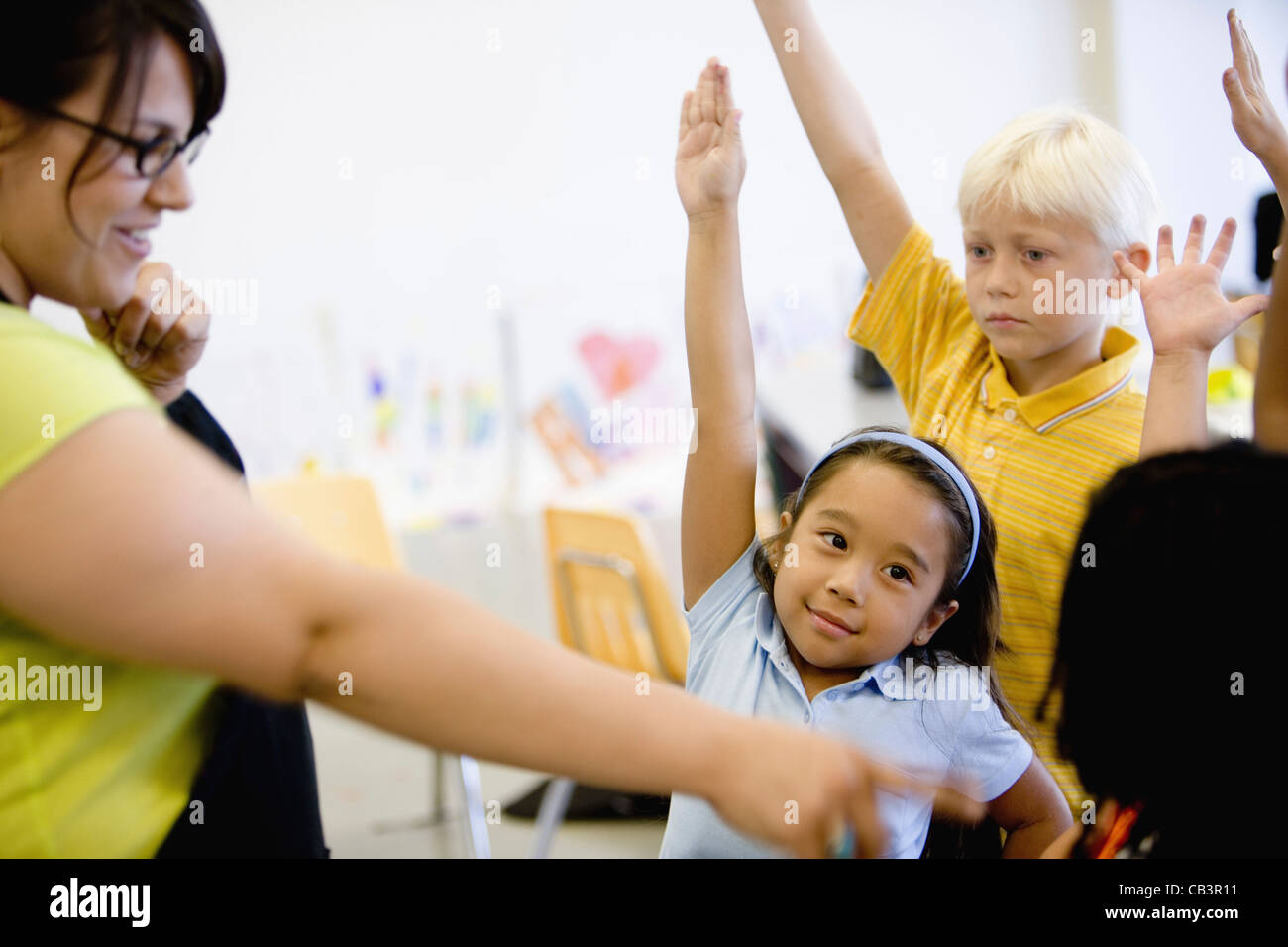 Teacher with her young students raising hands Stock Photo - Alamy