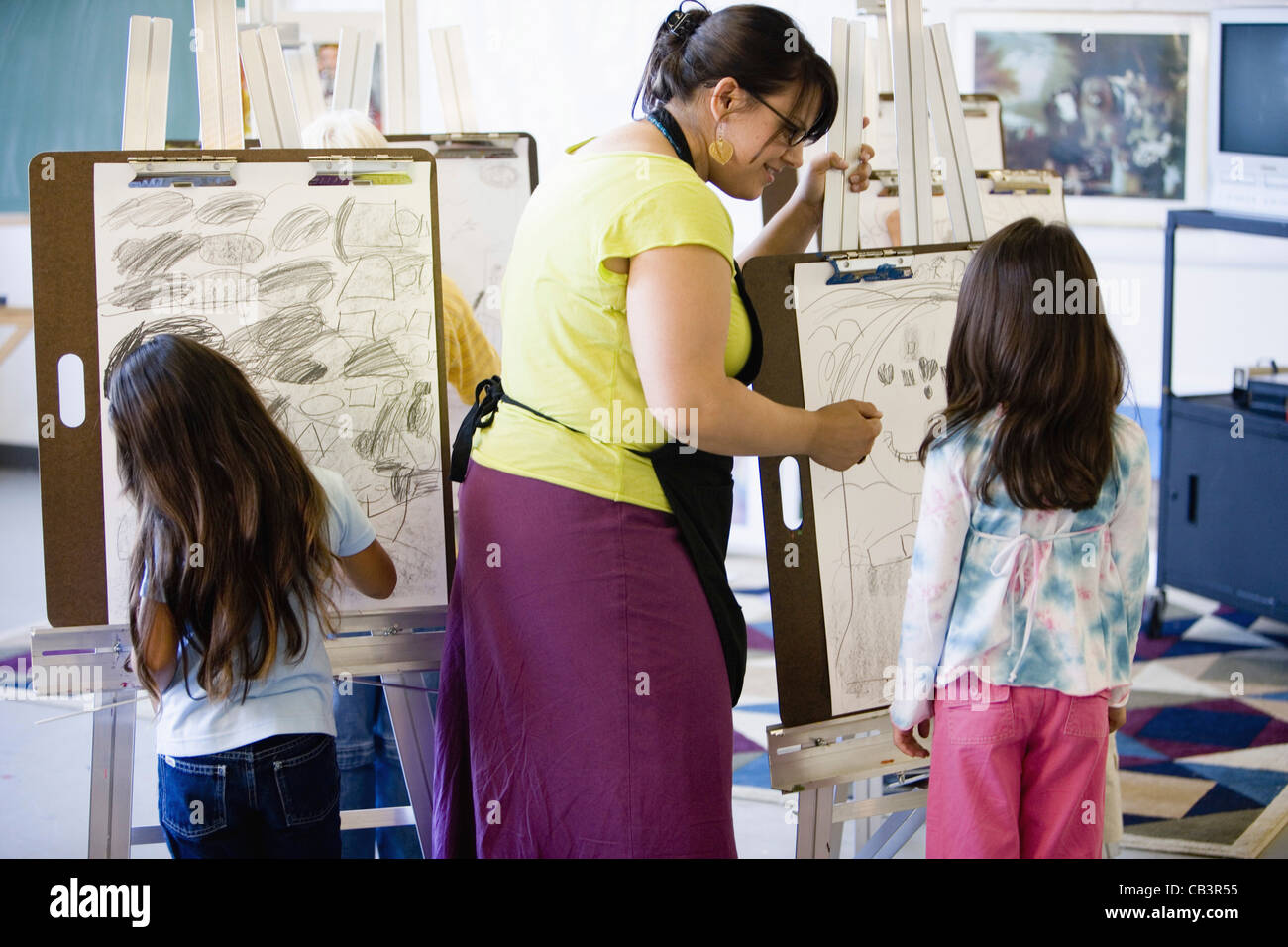 An art teacher showing young girls how to draw on an easel in art class ...