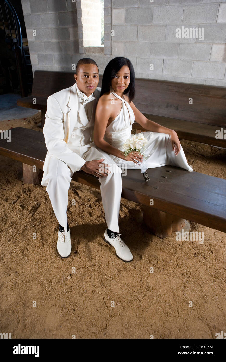 Portrait of bride and groom in white sitting on a bench inside a ...