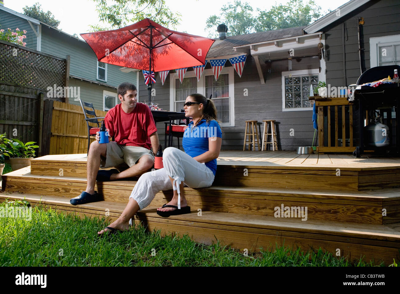Young couple sitting on steps of their backyard patio with 4th of July ...
