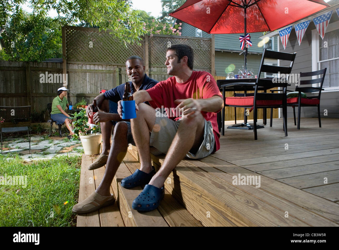 Two men sitting on steps of backyard patio, two women sitting in ...