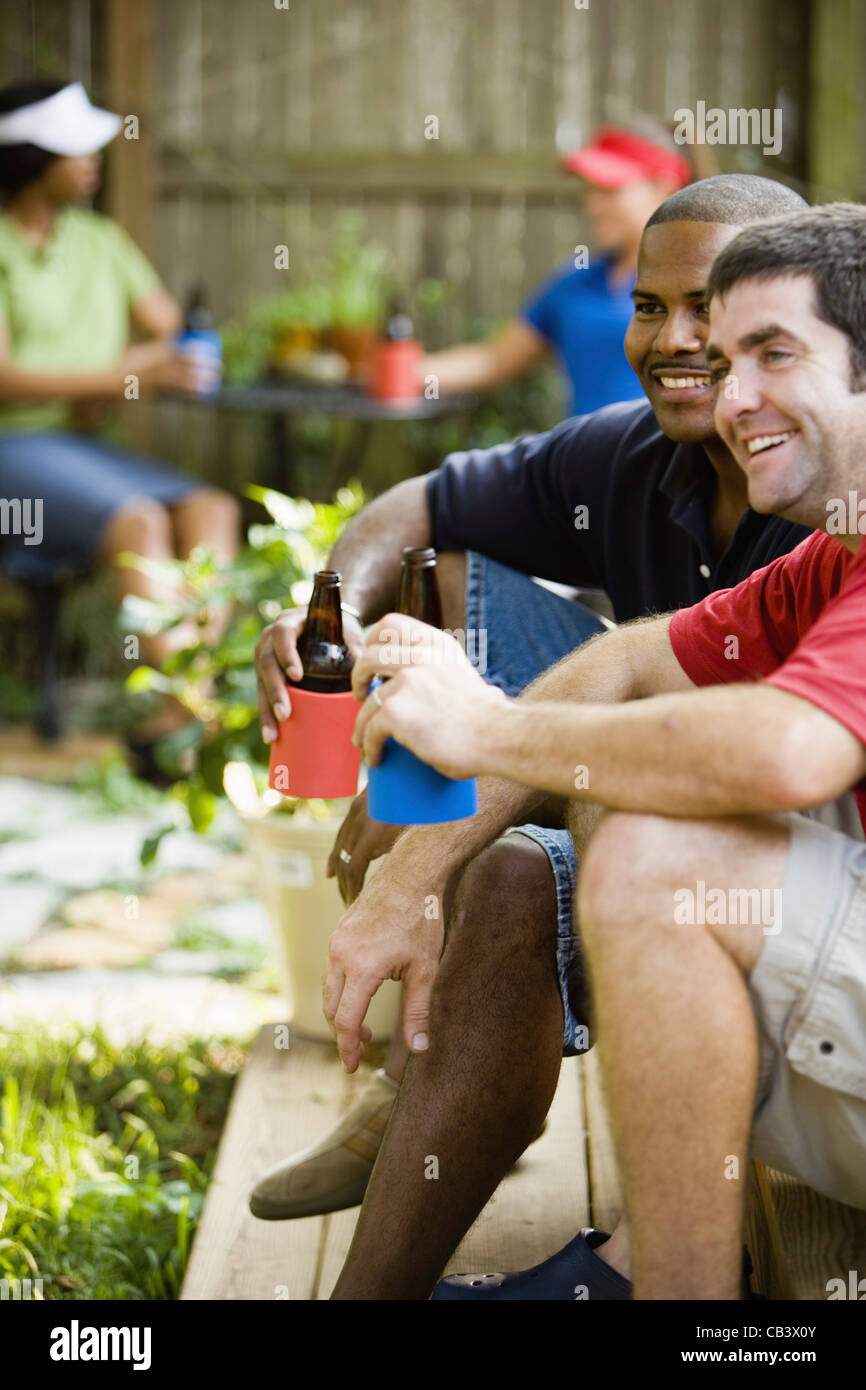 Two men sitting on steps of backyard patio enjoying cold beverages ...