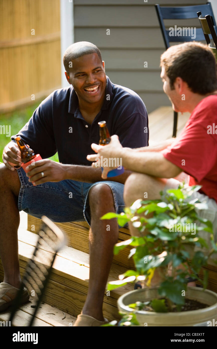 Two men sitting on steps of backyard patio enjoying cold beverages ...