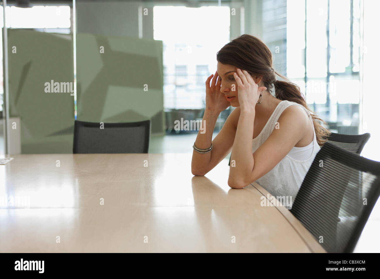 Woman sitting with head in hands at boardroom table Stock Photo - Alamy