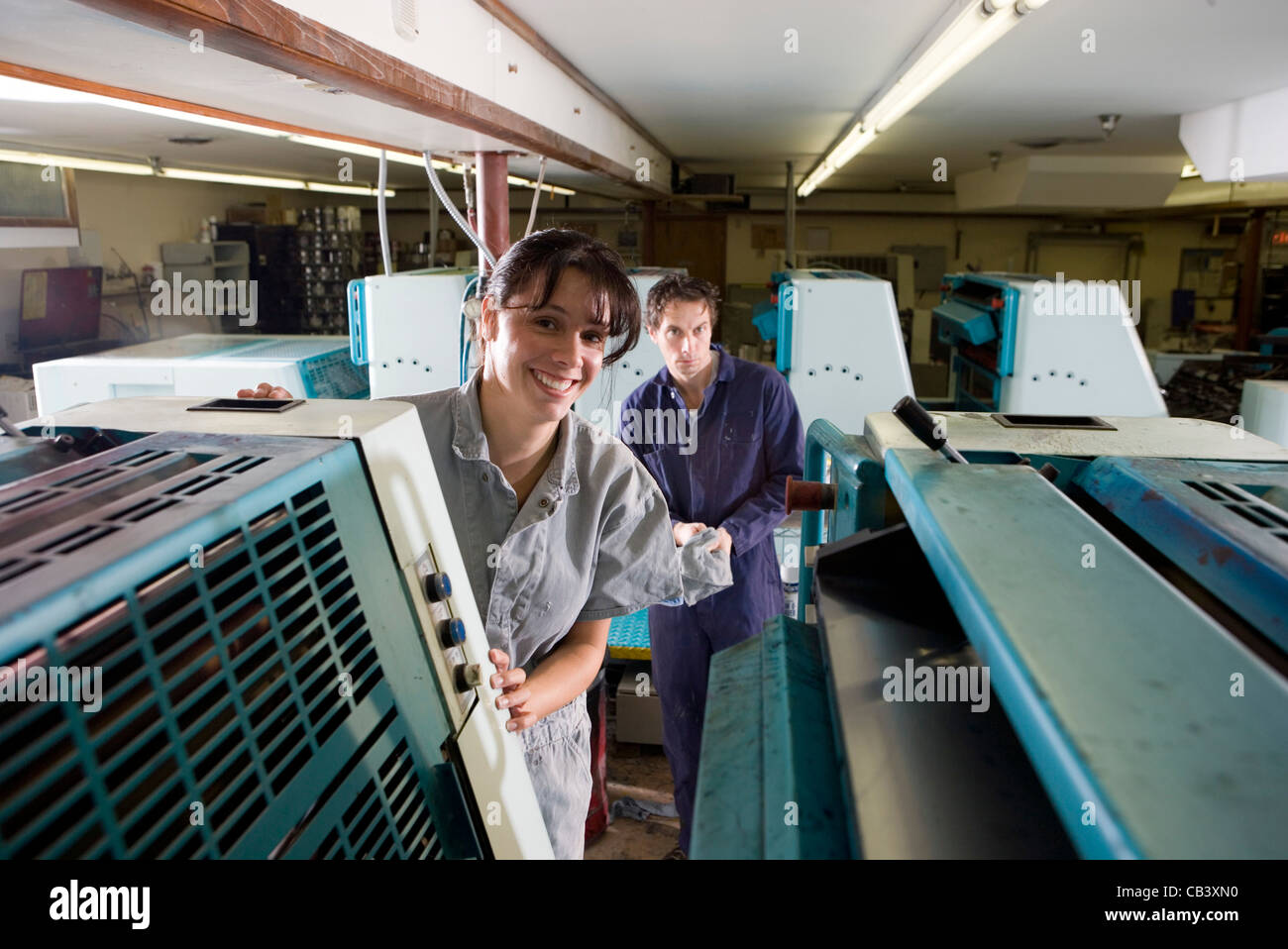 Portrait of a man and a woman in coveralls behind a printing machine ...