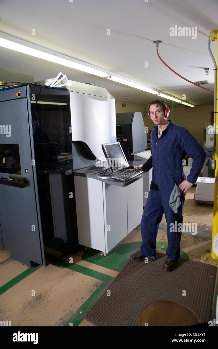 View of a man in coveralls operating a machine by using a computer ...