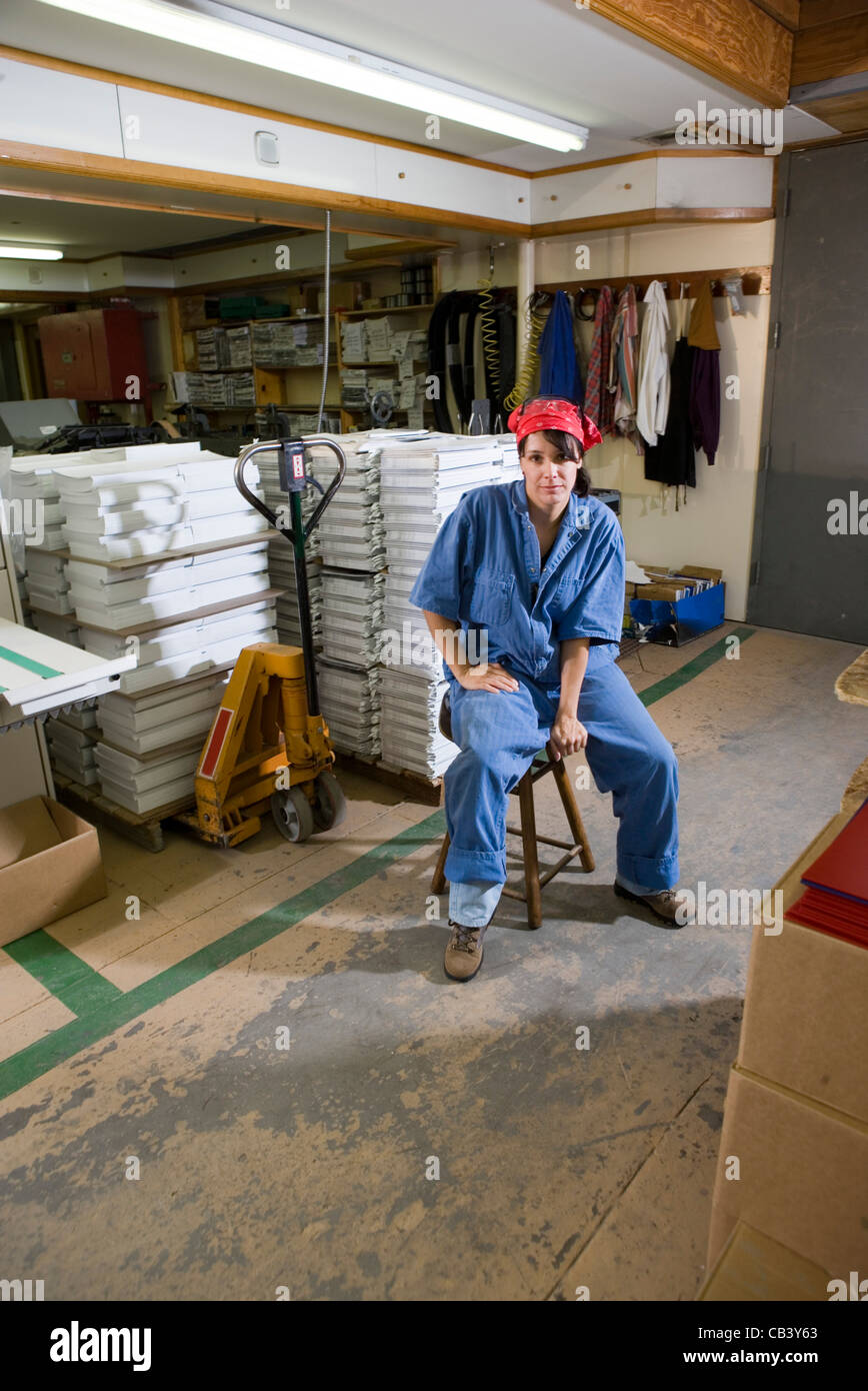Portrait of a woman sitting on a stool in a warehouse Stock Photo - Alamy