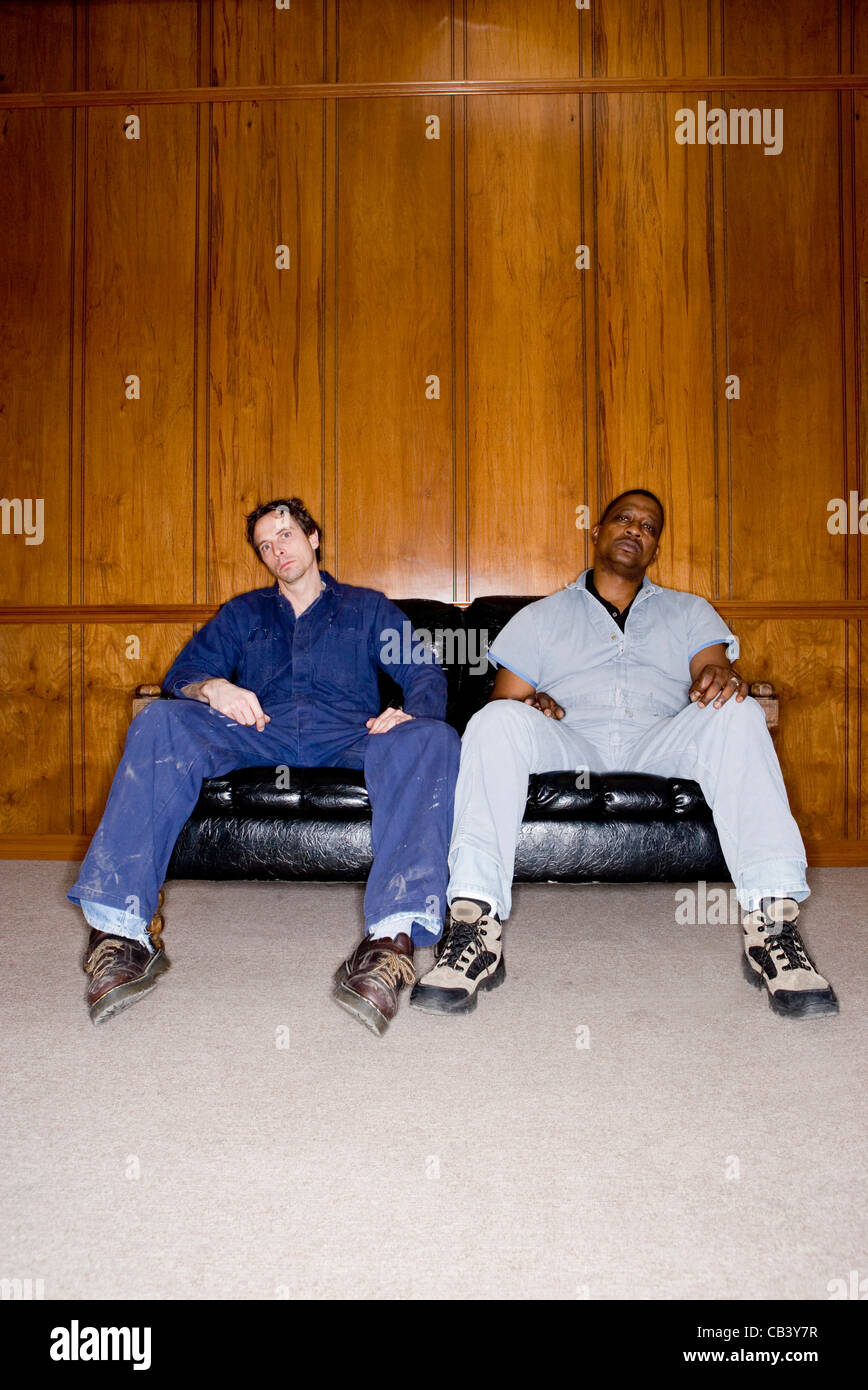 Portrait of two men in coveralls sitting on a sofa Stock Photo - Alamy
