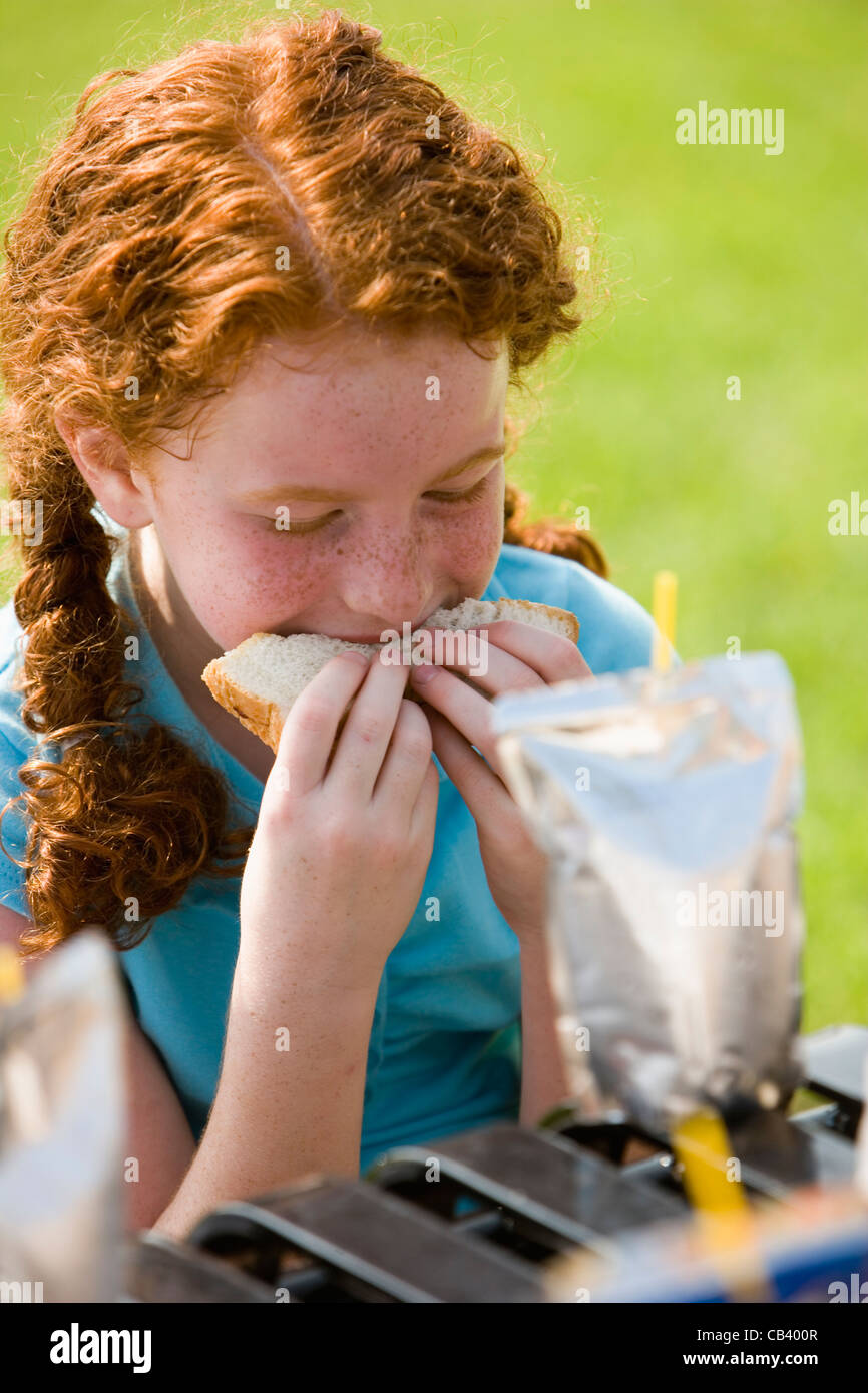 Close-up of girl biting into a sandwich at a picnic table Stock Photo ...