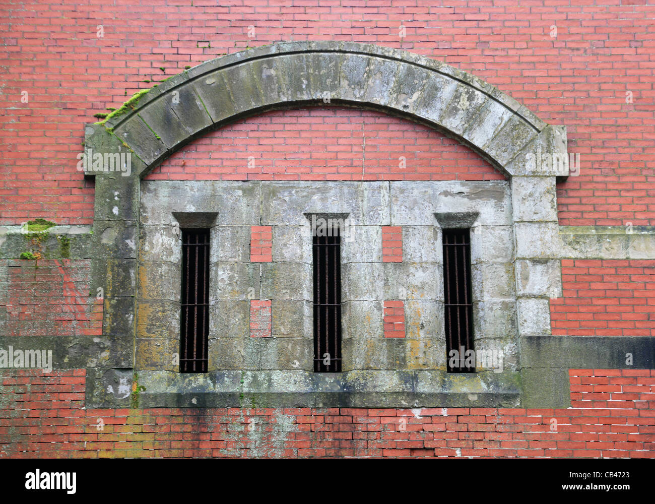 old weathered and mossy brick wall with stone arch and narrow barred ...