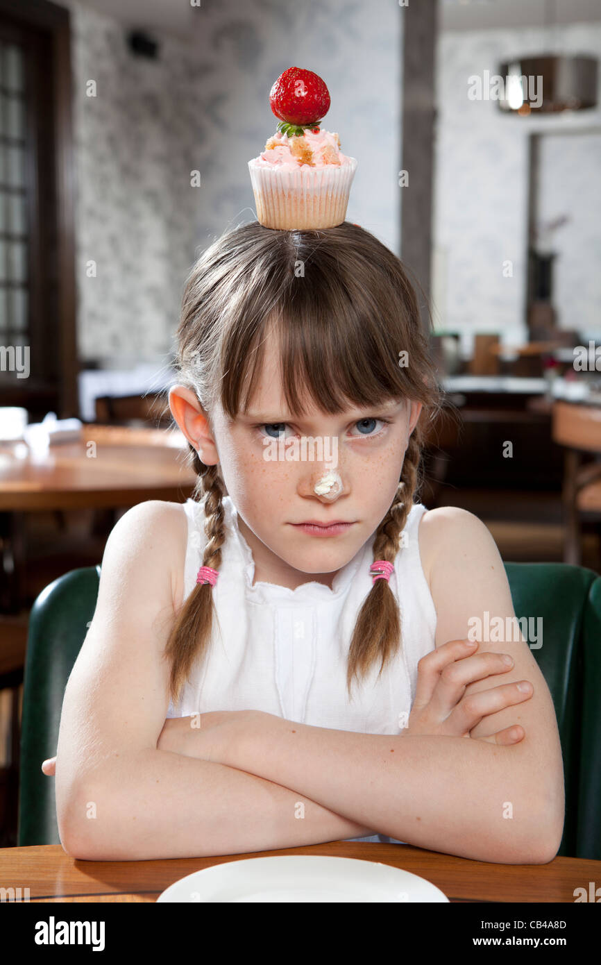 Grumpy girl with cupcake on head in posh high tea hotel Stock Photo - Alamy