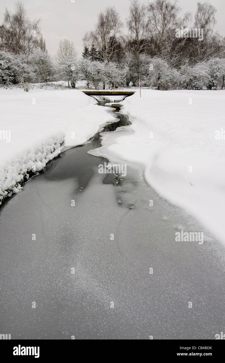 A frozen stream meanders its way through a snow covered golf course ...