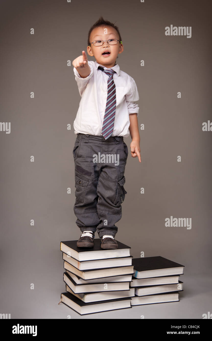 A kid playing a stock trader making a bid standing on pile of books ...