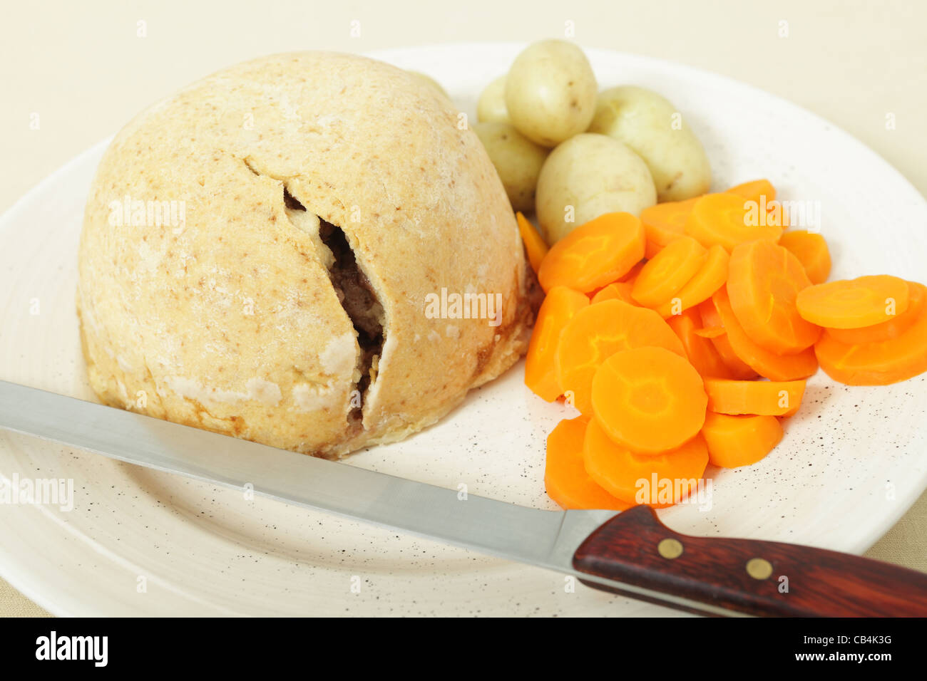 A steak and kidney pudding ready to cut open on a serving platter with ...