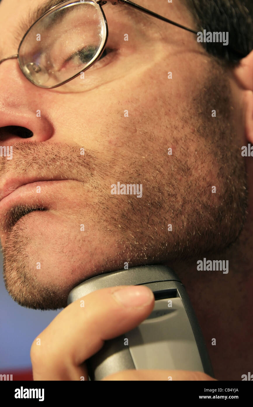 a man shaving his chin with a silver electric razor Stock Photo - Alamy