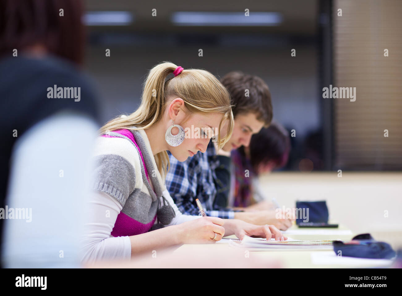 young, pretty female college student sitting in a classroom full of ...