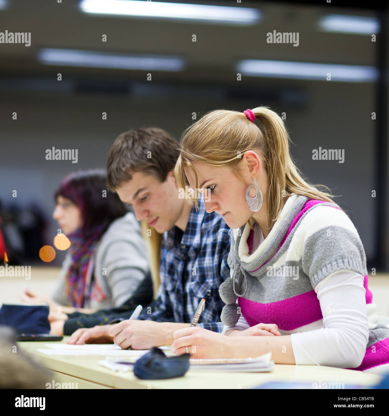 young, pretty female college student sitting in a classroom full of ...