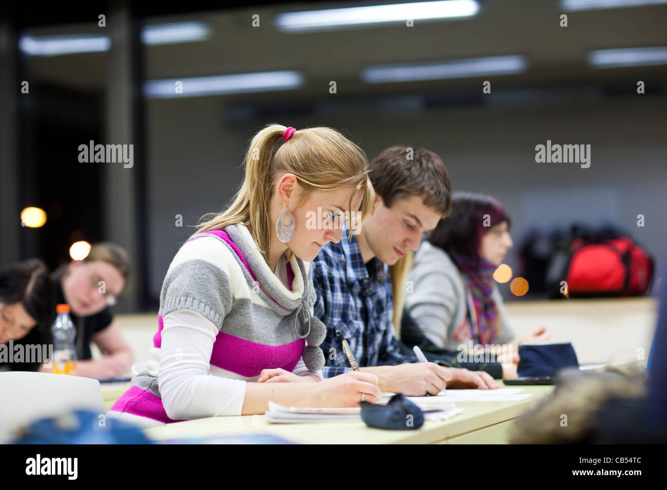 young, pretty female college student sitting in a classroom full of ...