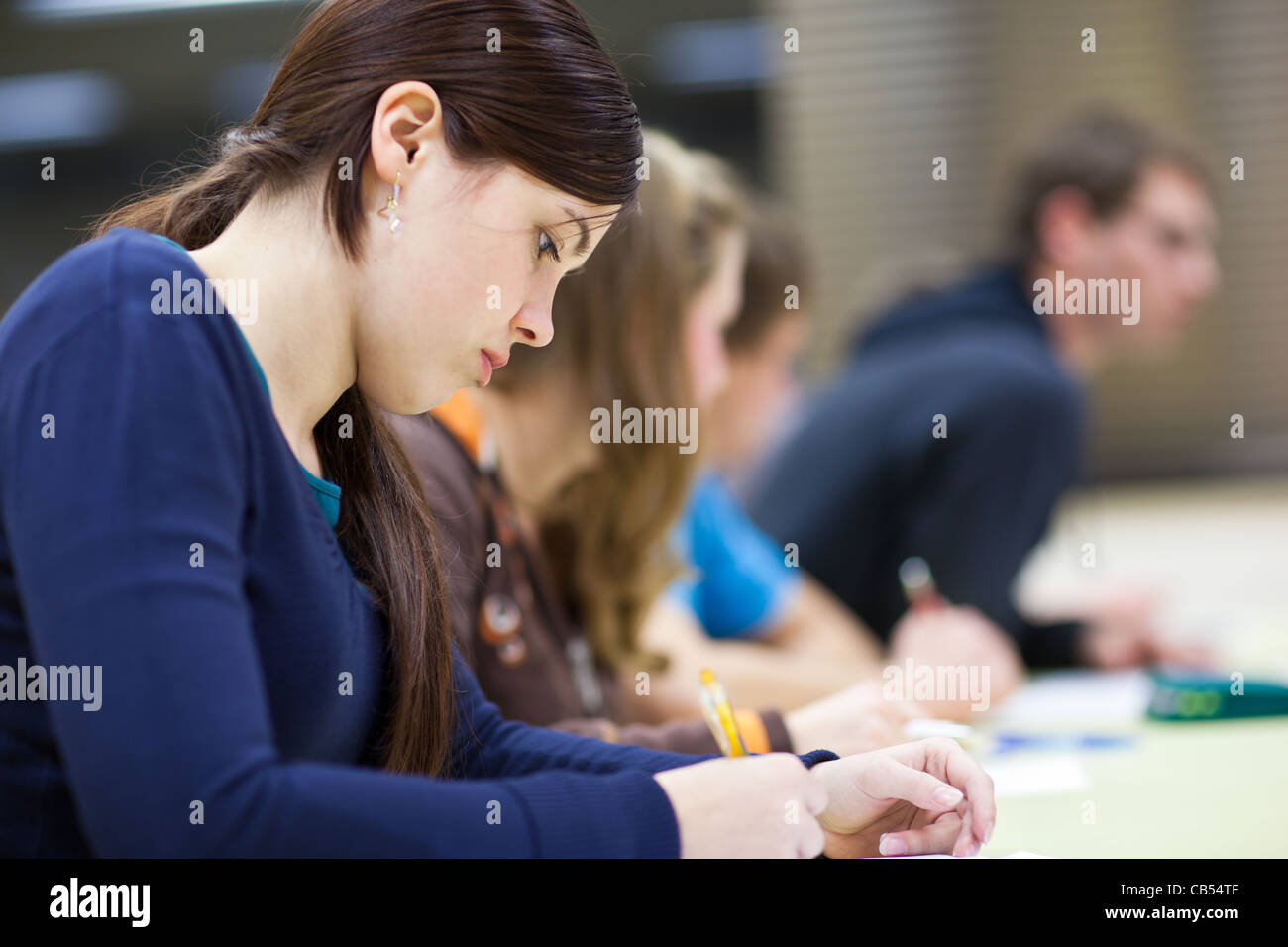 young, pretty female college student sitting in a classroom full of ...