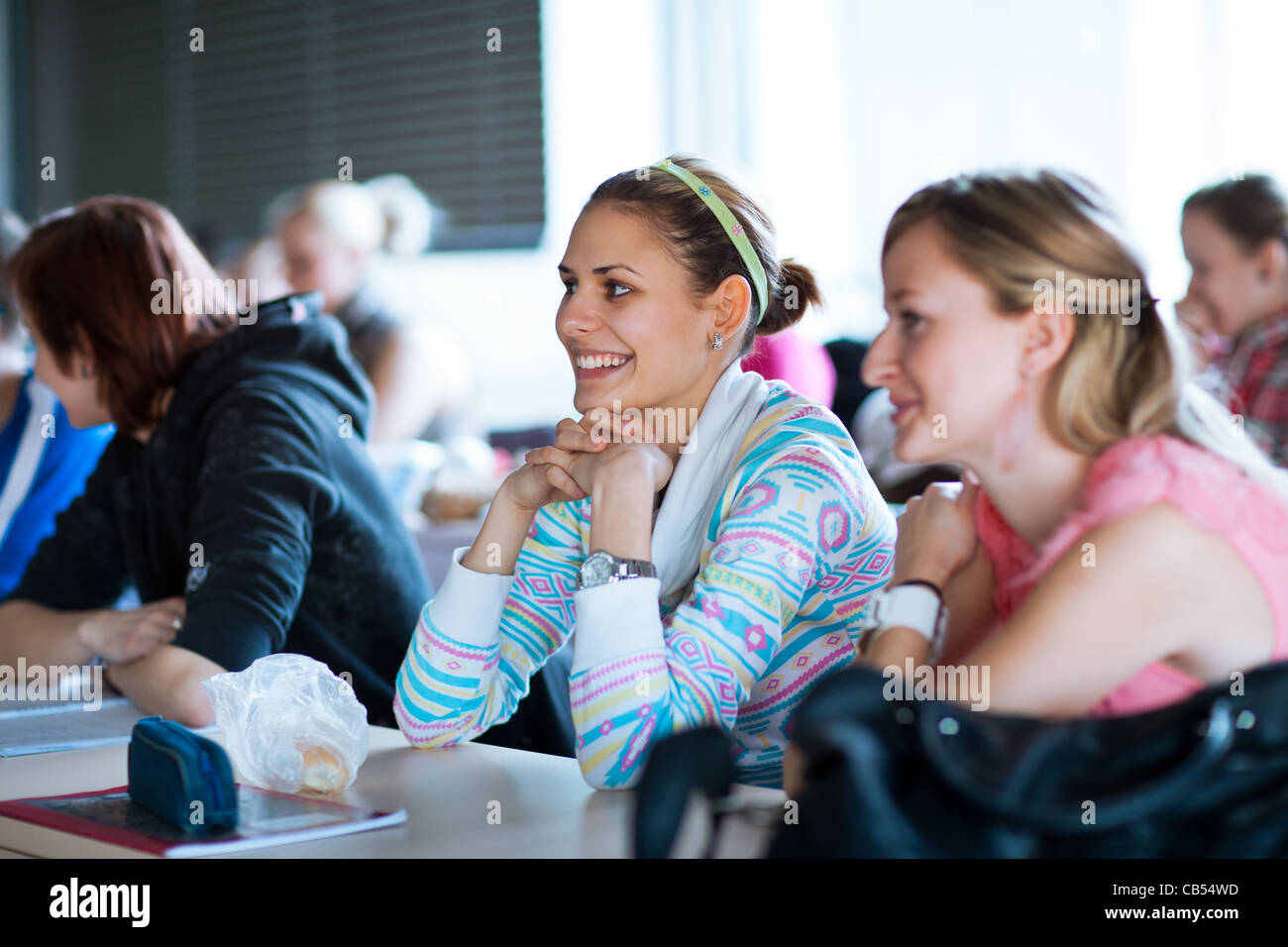 young, pretty female college student sitting in a classroom full of ...