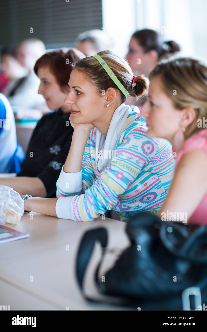 young, pretty female college student sitting in a classroom full of ...