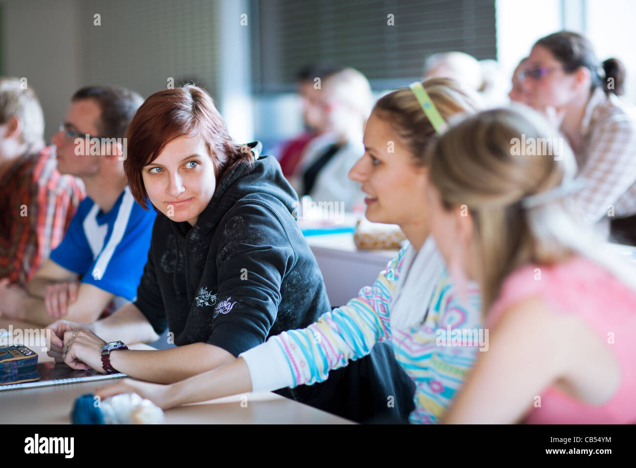 young, pretty female college student sitting in a classroom full of ...