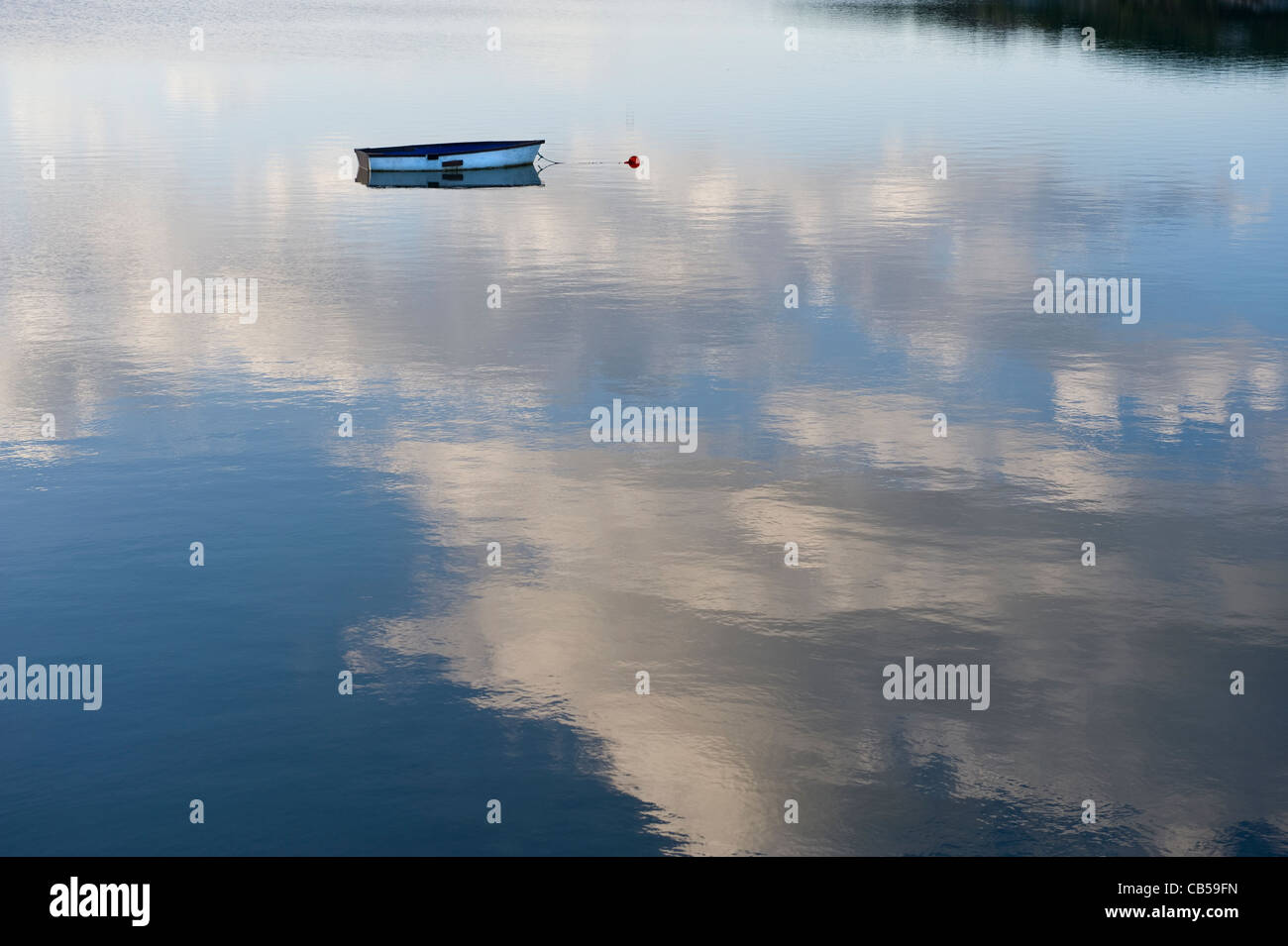 Single row boat on the water with reflection of blue sky and clouds ...