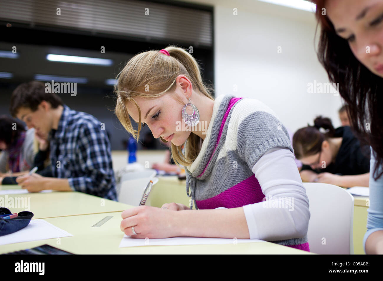 pretty female college student sitting in a classroom full of students ...