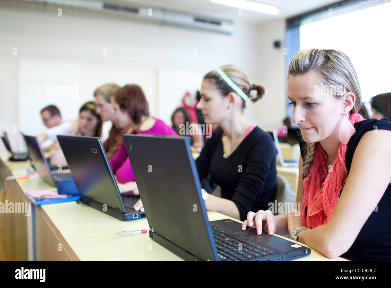 college students sitting in a classroom, using laptop computers during ...