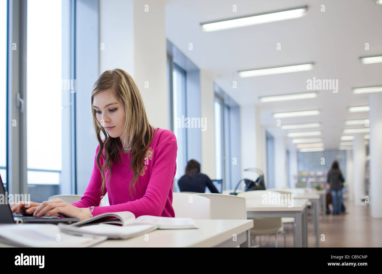 in the library - pretty, female student with laptop and books working ...