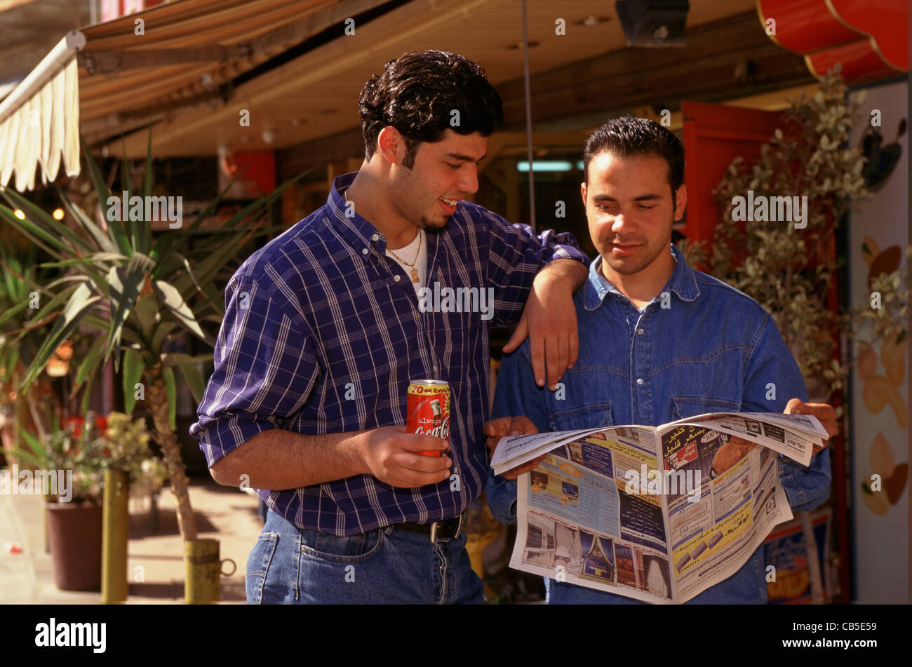Two friends read a newspaper while one drinks an can of coke, Beruit ...