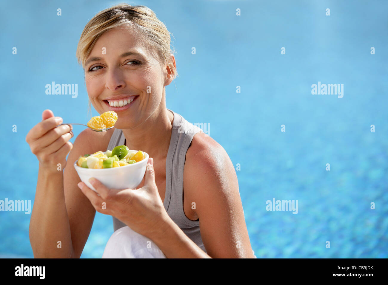 Woman eating fruit cocktail by swimming pool Stock Photo - Alamy