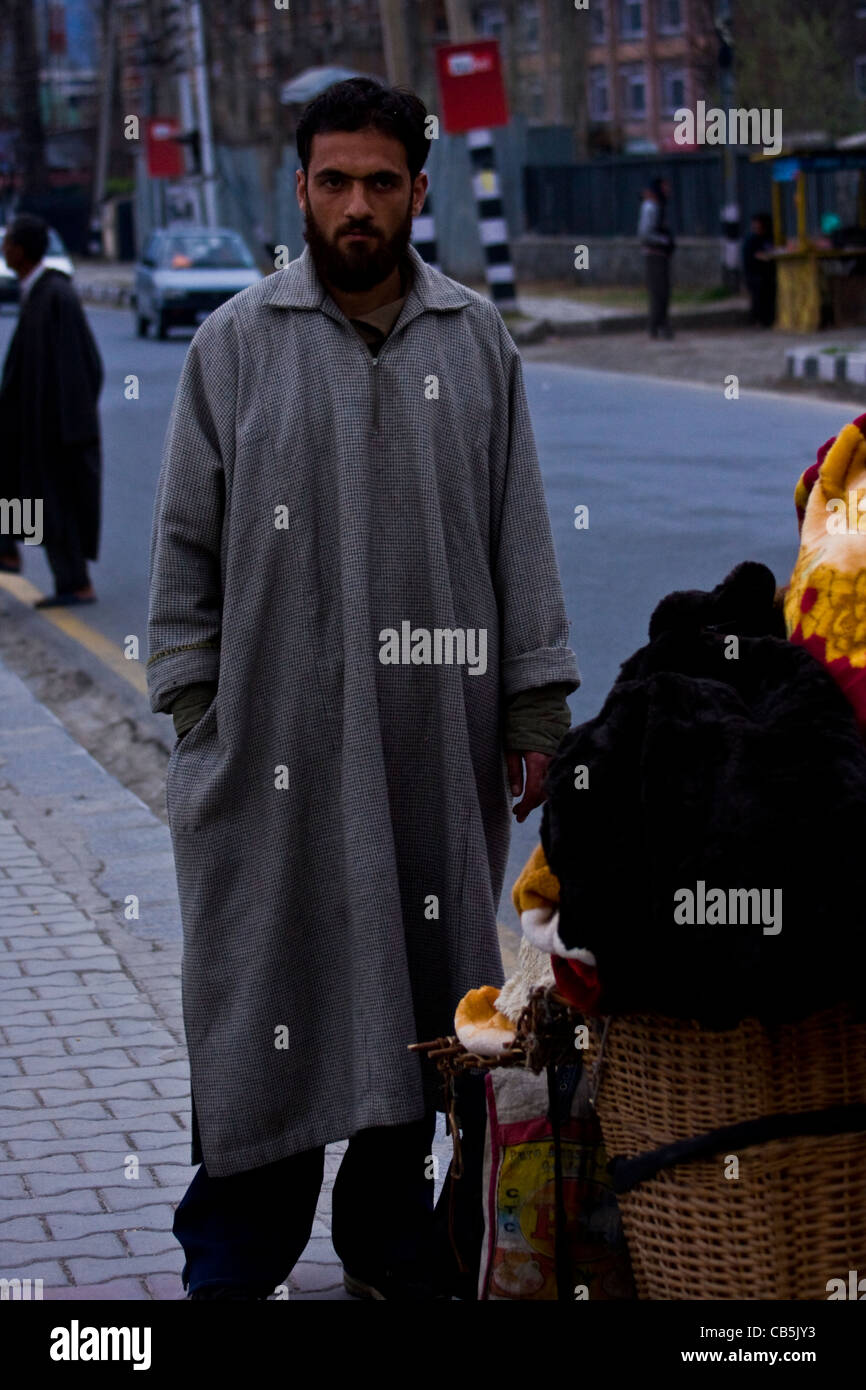 A Kashmiri man in traditional cloth selling things on the footpath ...
