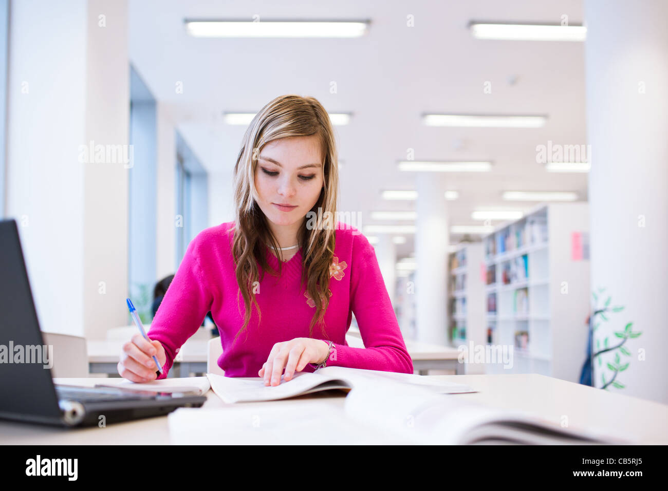 in the library - pretty, female student with laptop and books working ...