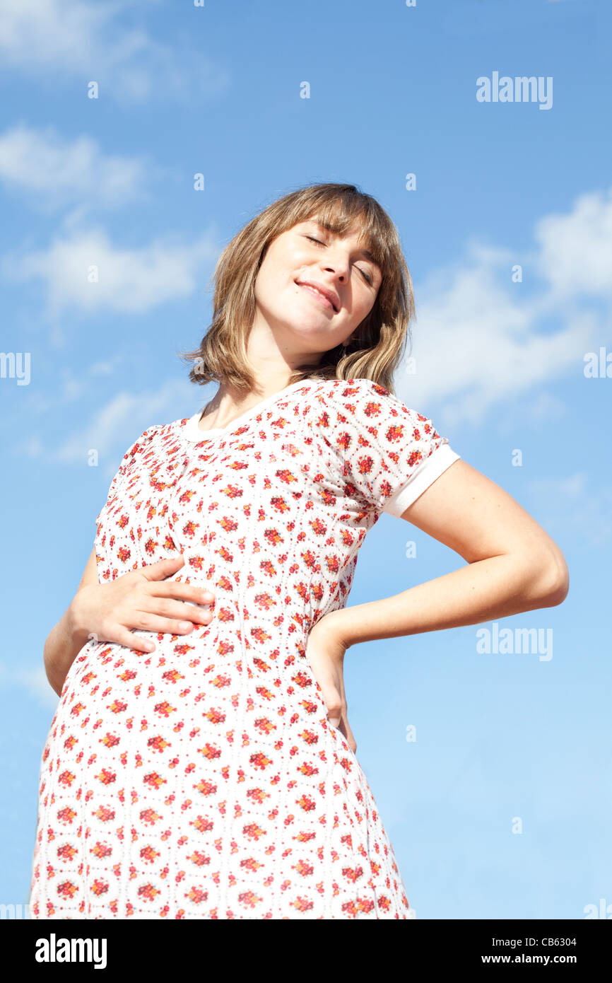 young pregnant woman holding belly, eyes closed against blue sky, low ...
