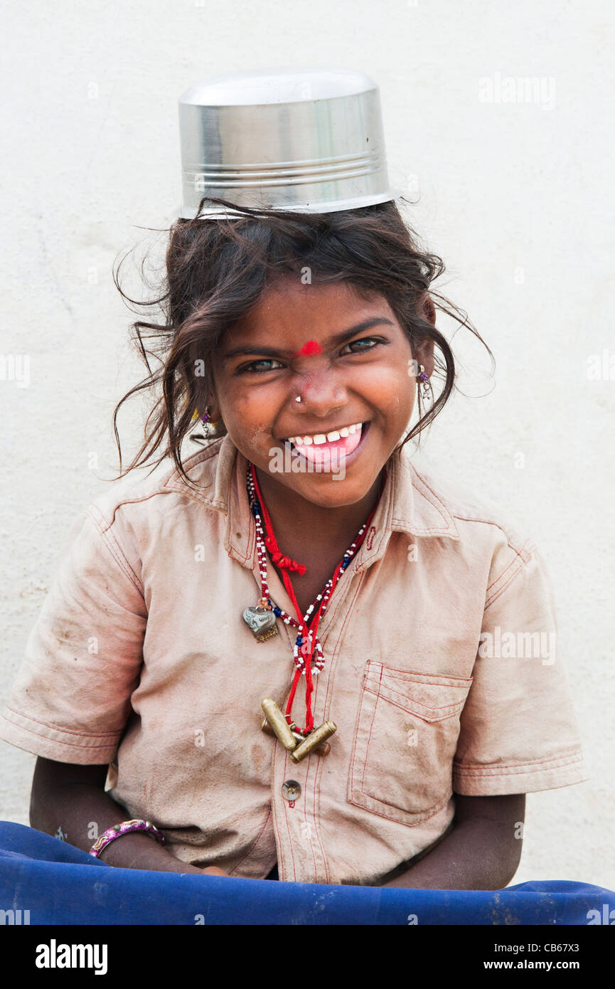 Smiling happy poor Indian beggar girl with a metal pot on her head ...
