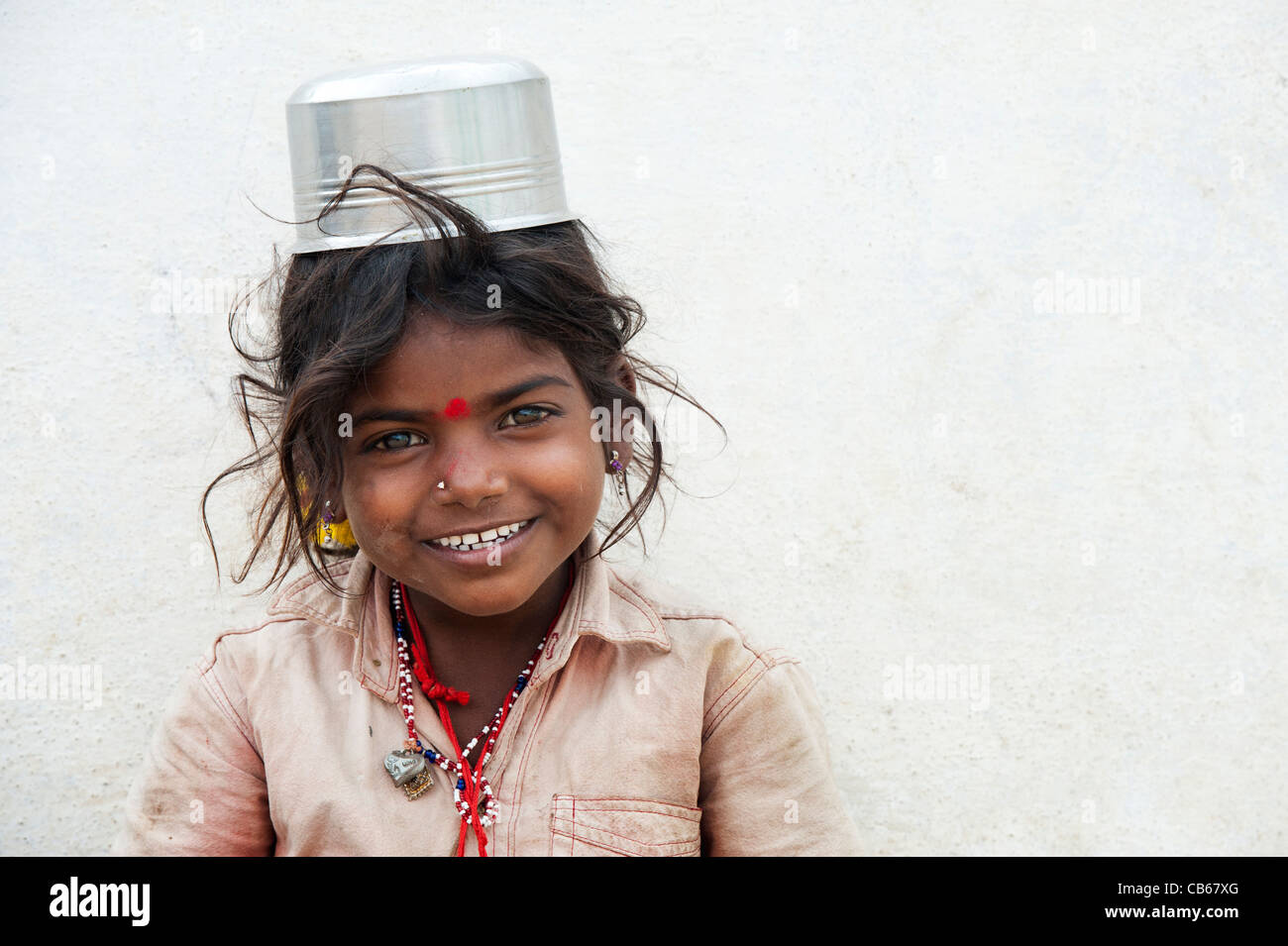 Smiling happy poor Indian beggar girl with a metal pot on her head ...