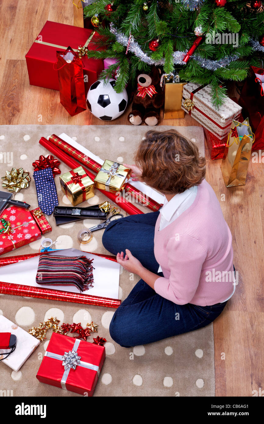 Overhead photo of a woman sat on a rug at home wrapping her Christmas ...
