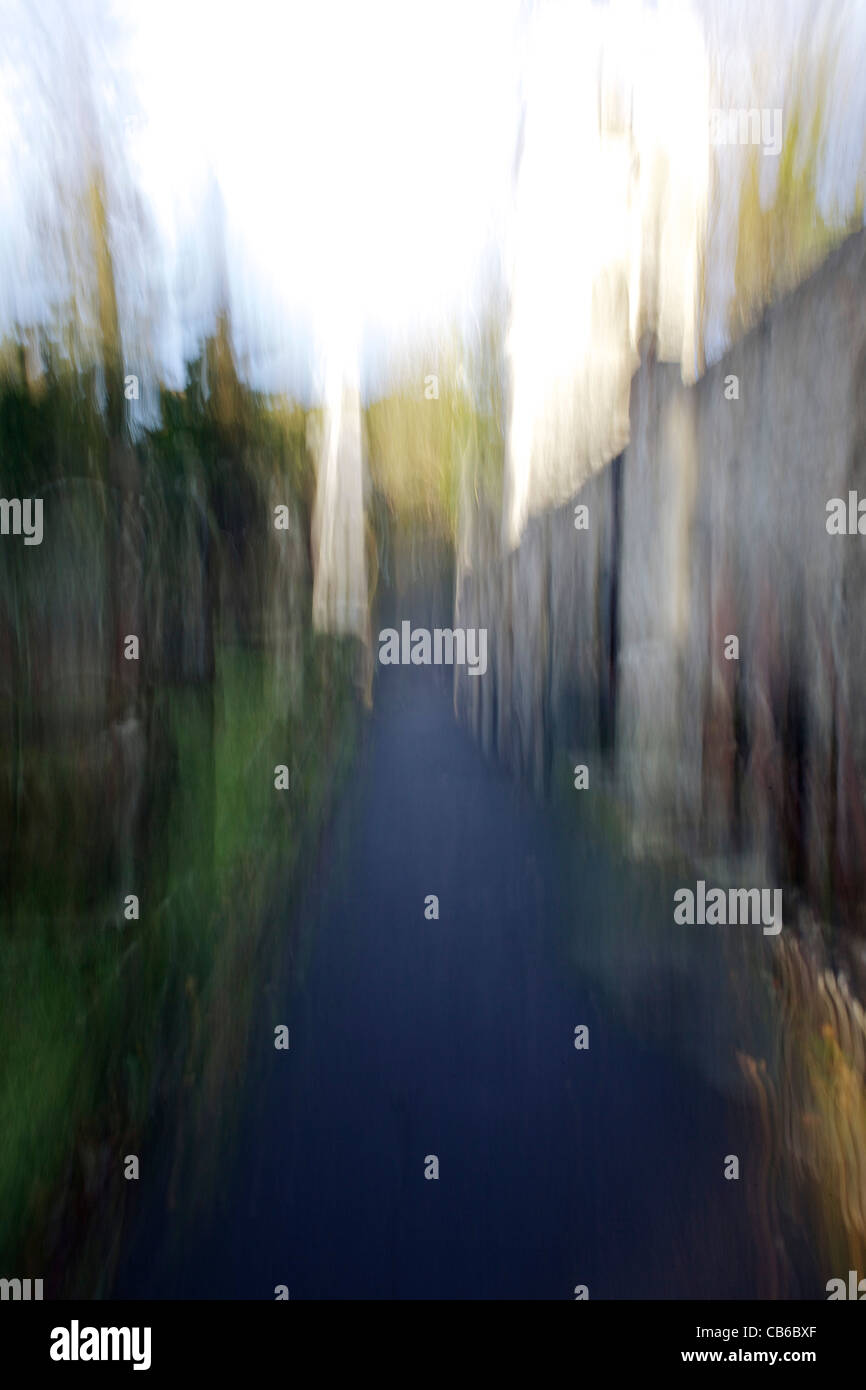 Blurred image of path with tall building on one side and trees on other ...