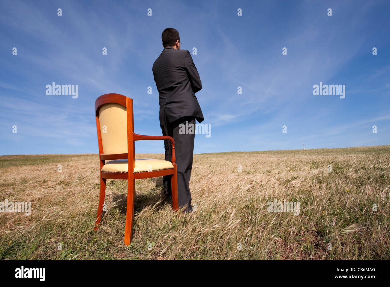businessman standing next to a chair in outdoor looking to the field ...