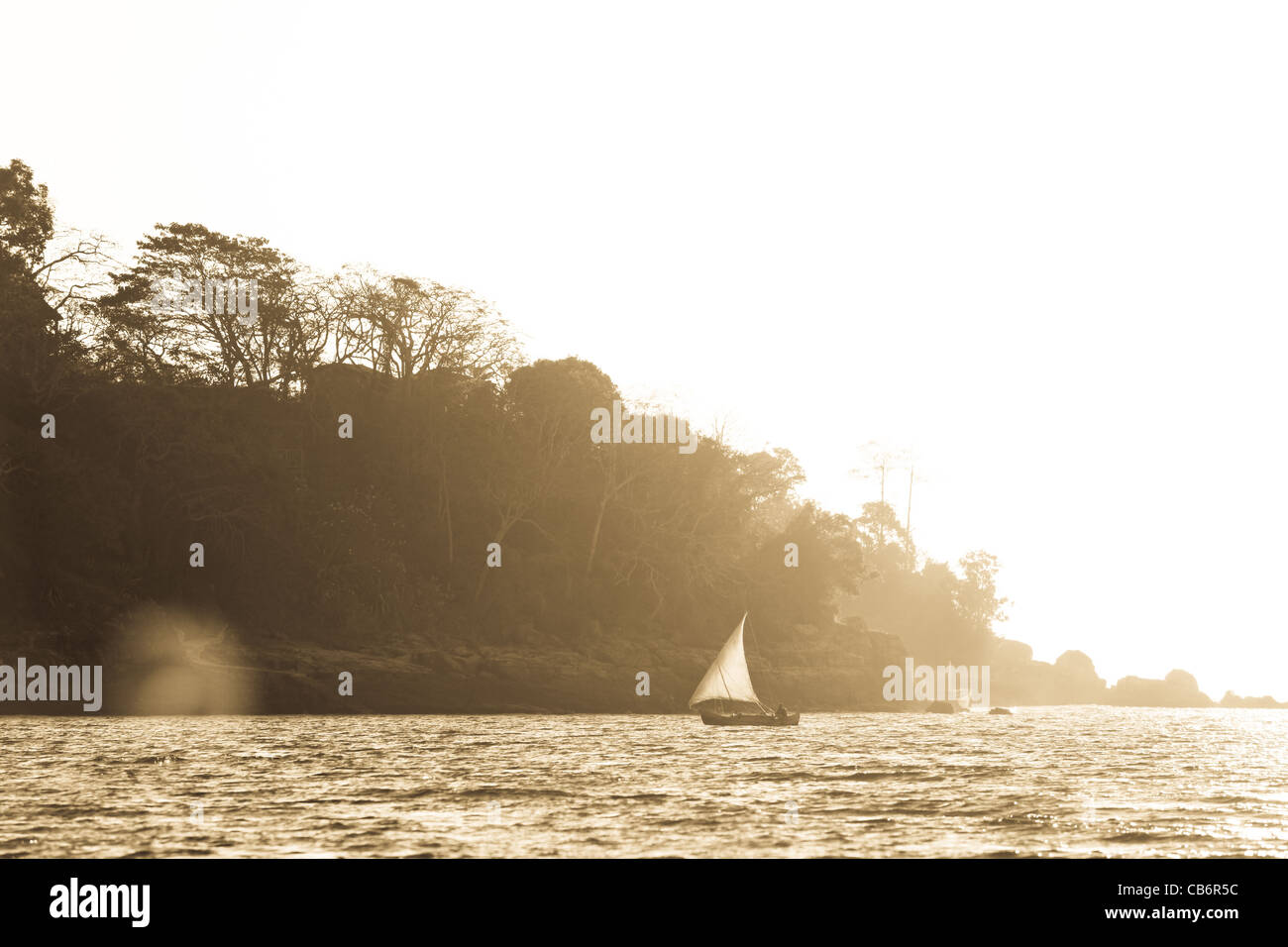 A traditional outrigger dugout canoe sailing at sunset off Ankify, near ...